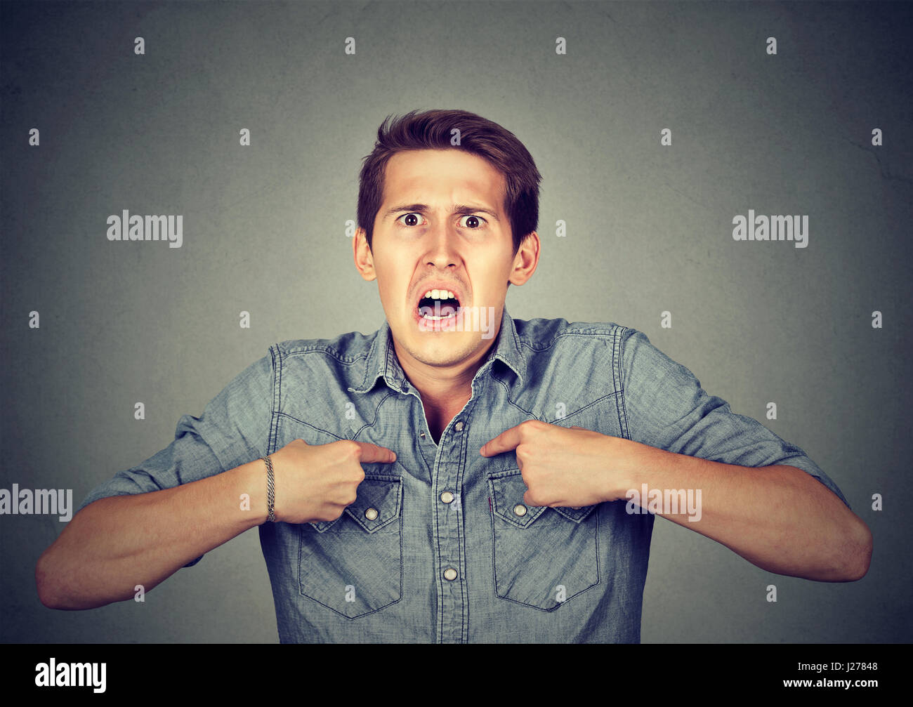 Angry, mad, unhappy young guy pointing at himself asking you mean me ...