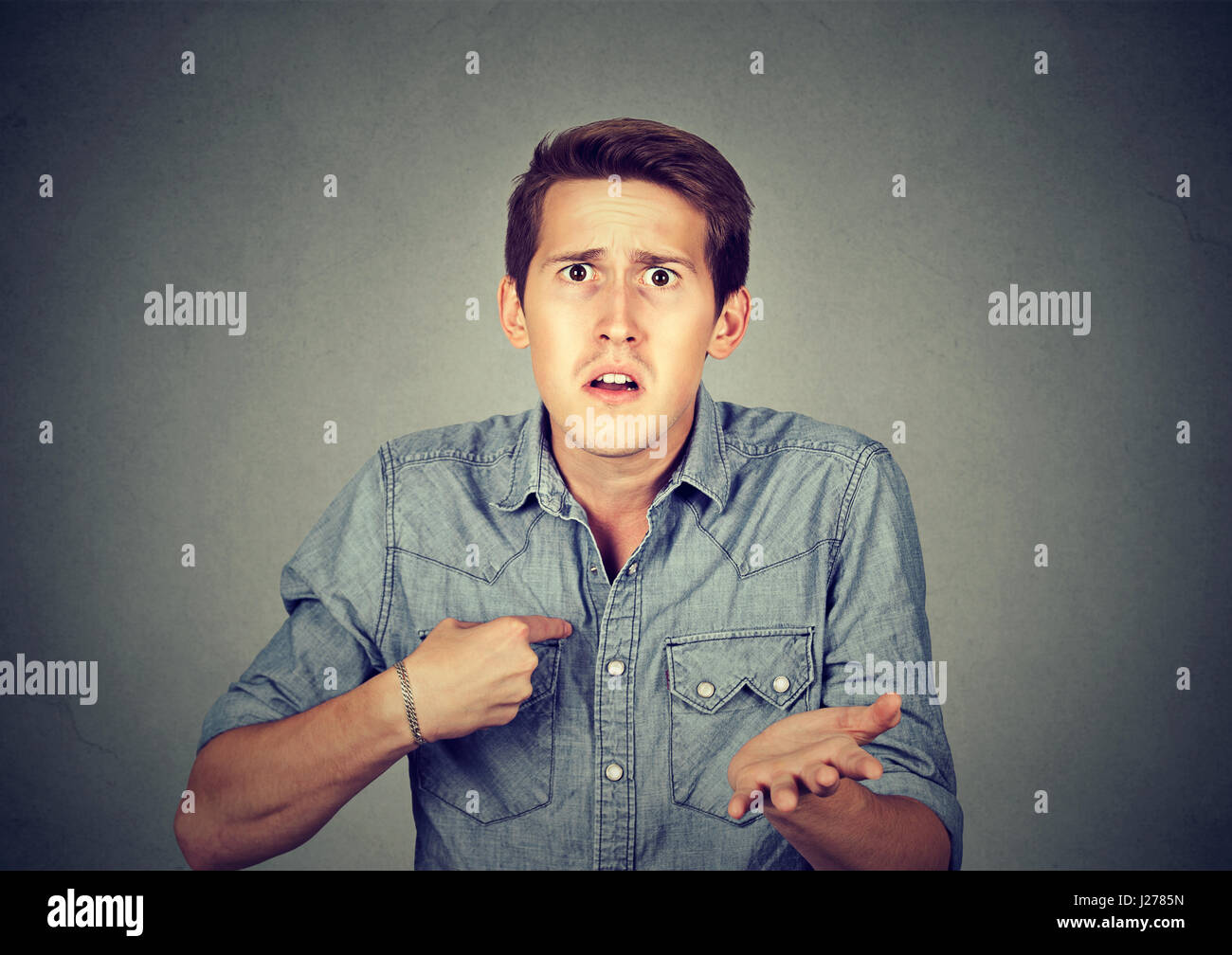 Angry, mad, unhappy young guy pointing at himself asking you mean me ...