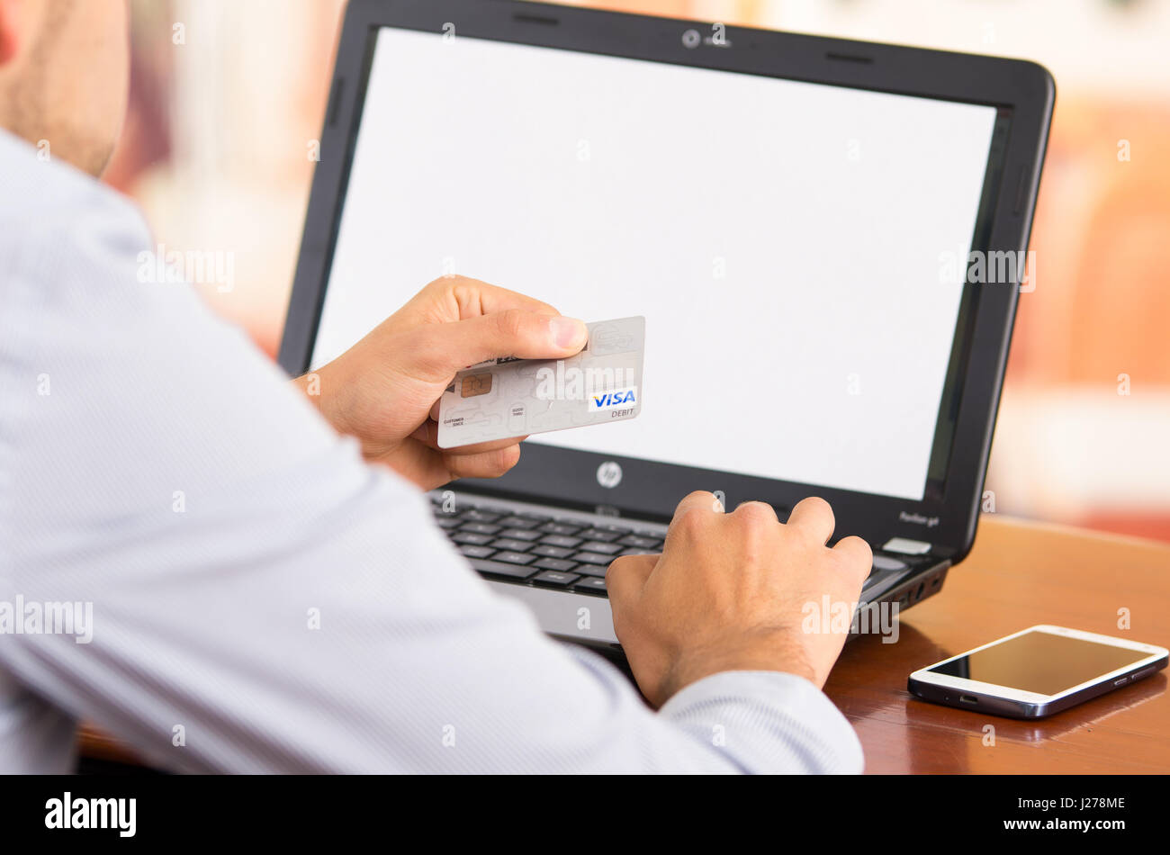 Closeup of man sitting by desk with laptop computer holding up Visa ...
