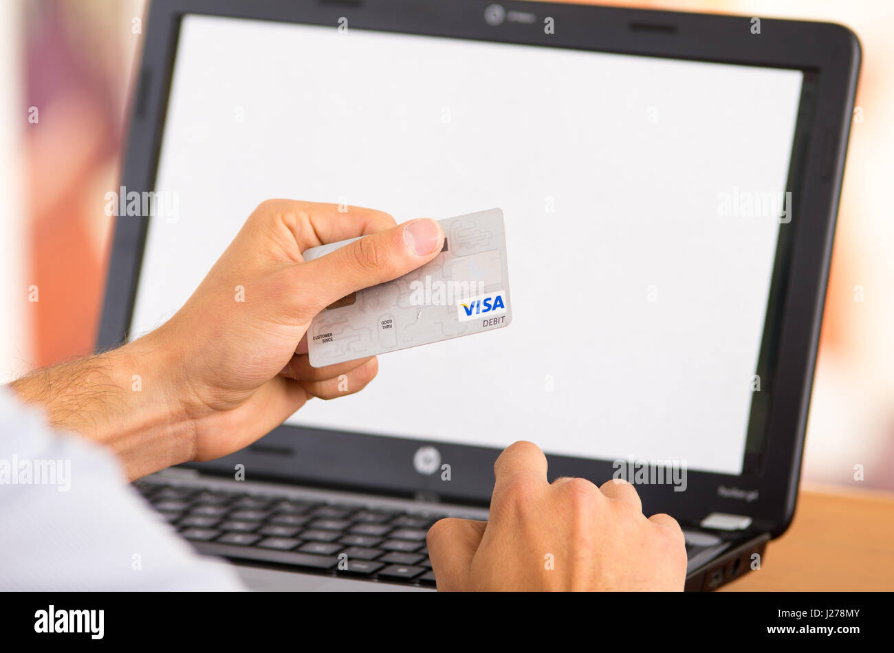 Closeup of man sitting by desk with laptop computer holding up Visa ...