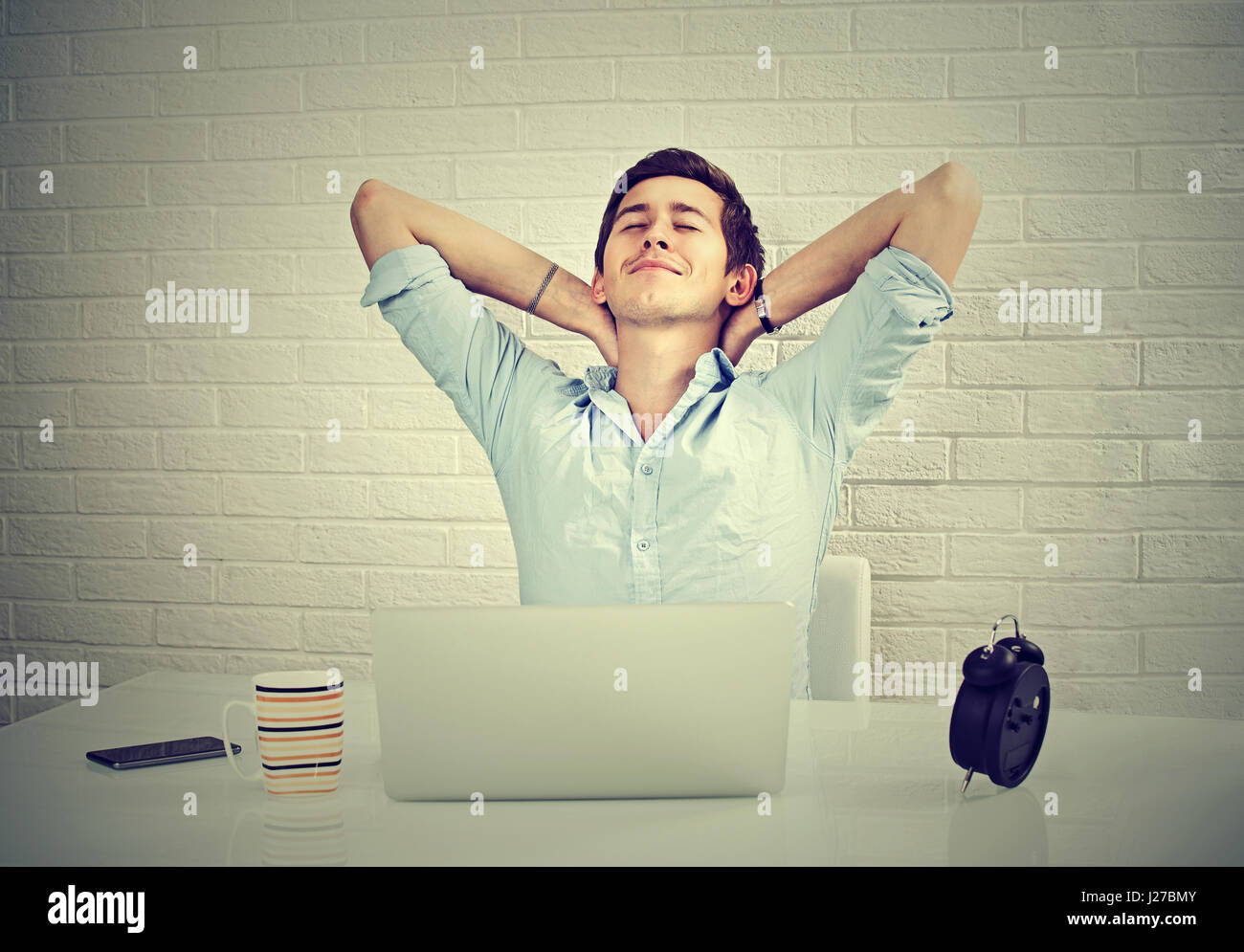 Relaxed young man with laptop computer sitting at his desk on white ...