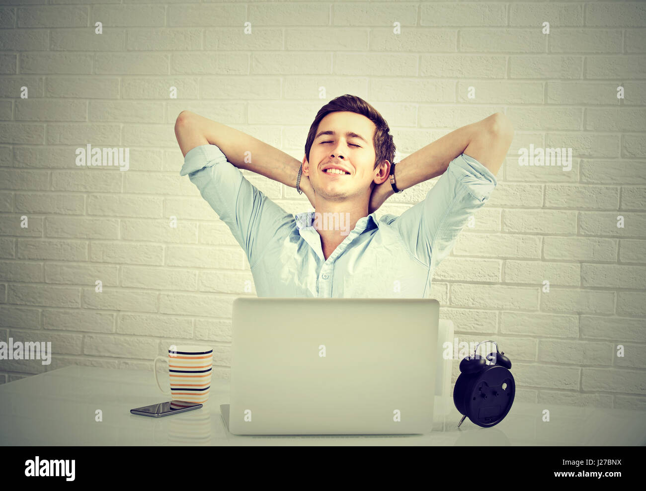 Relaxed young man with laptop computer sitting at his desk on white ...