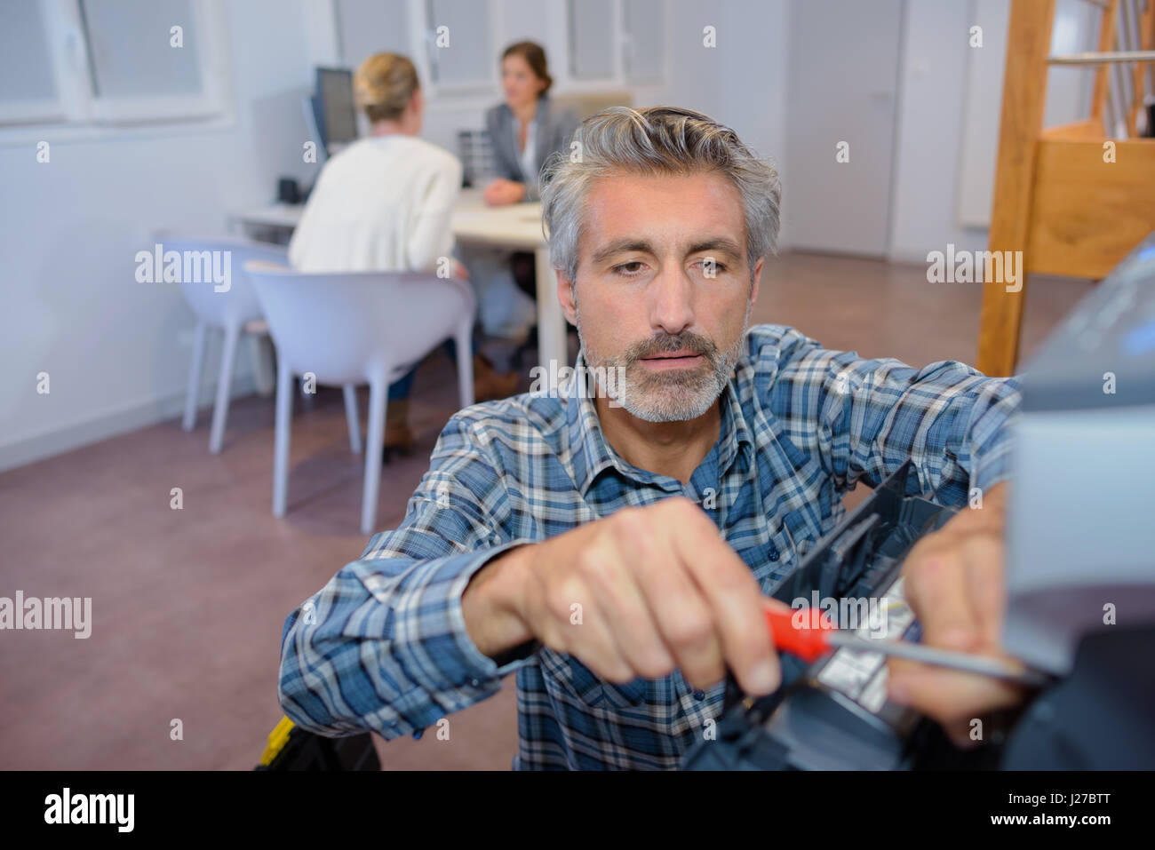 Man repairing office equipment, meeting in background Stock Photo - Alamy
