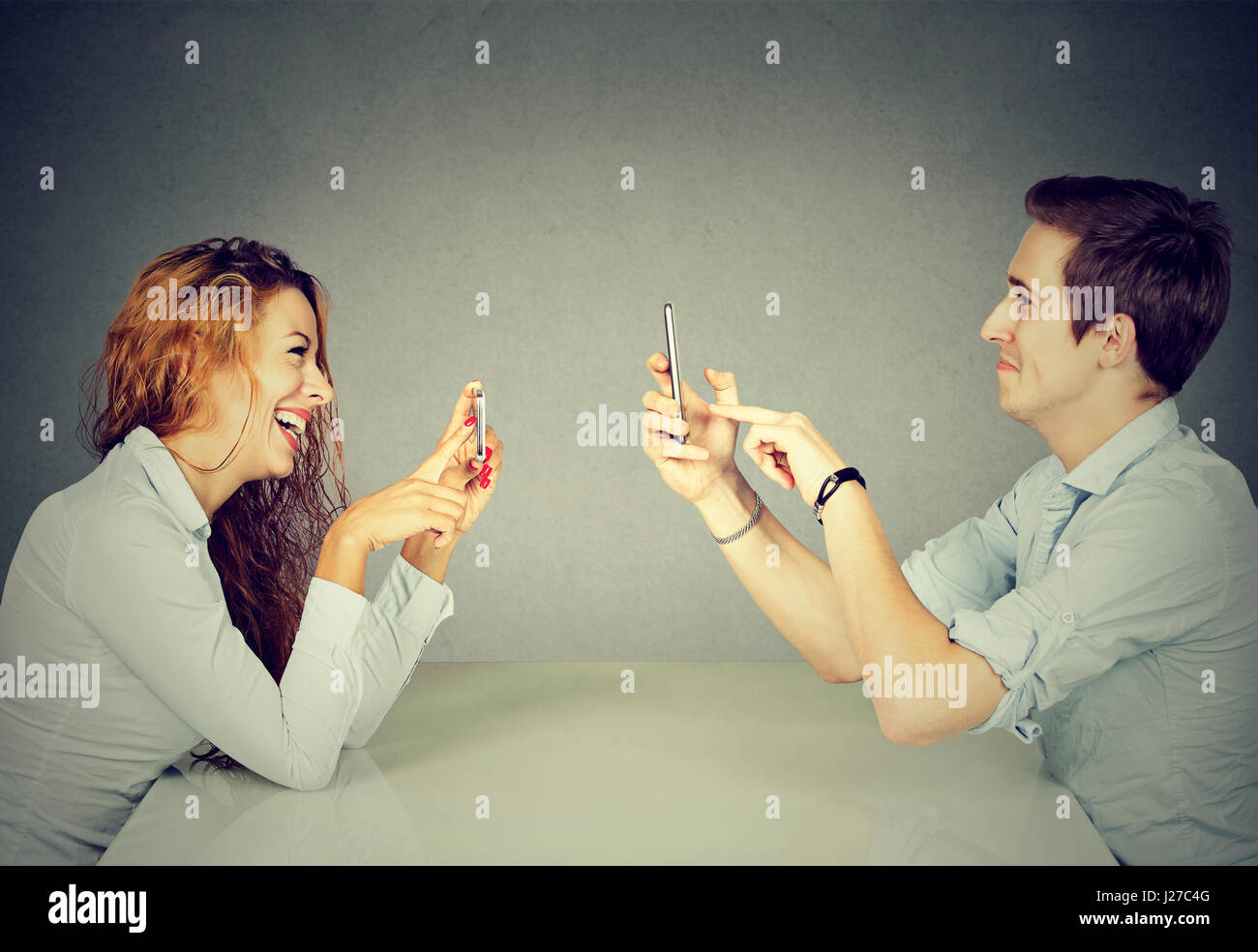Young man and woman sitting at table using mobile phones, texting via ...