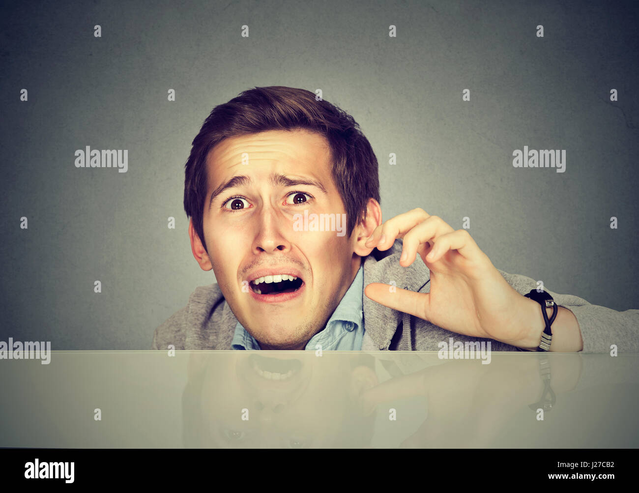 Funny scared man peeking from behind the desk isolated on gray ...