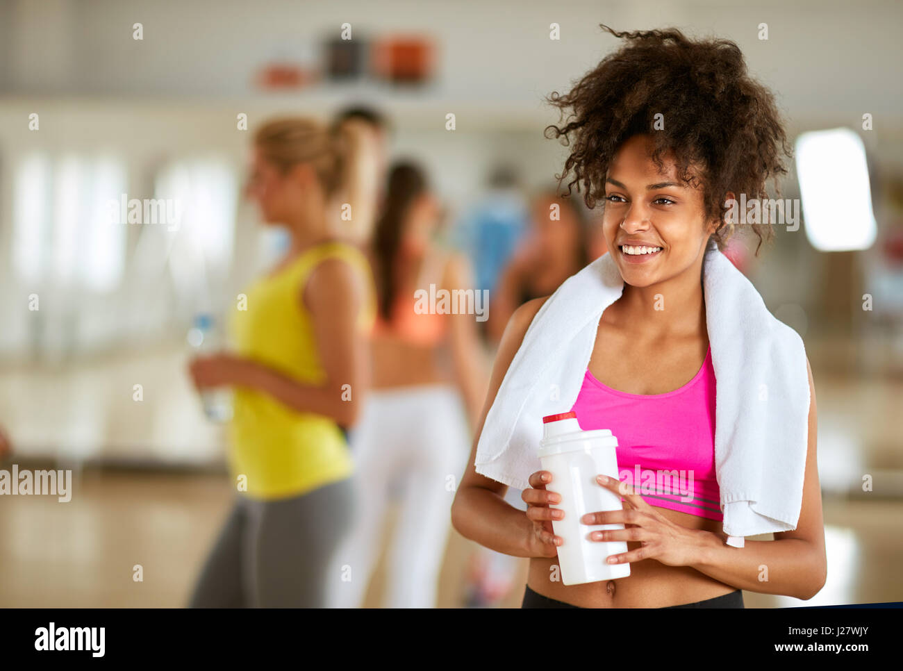 Young half-caste female smiling and refreshing with protein shake after ...