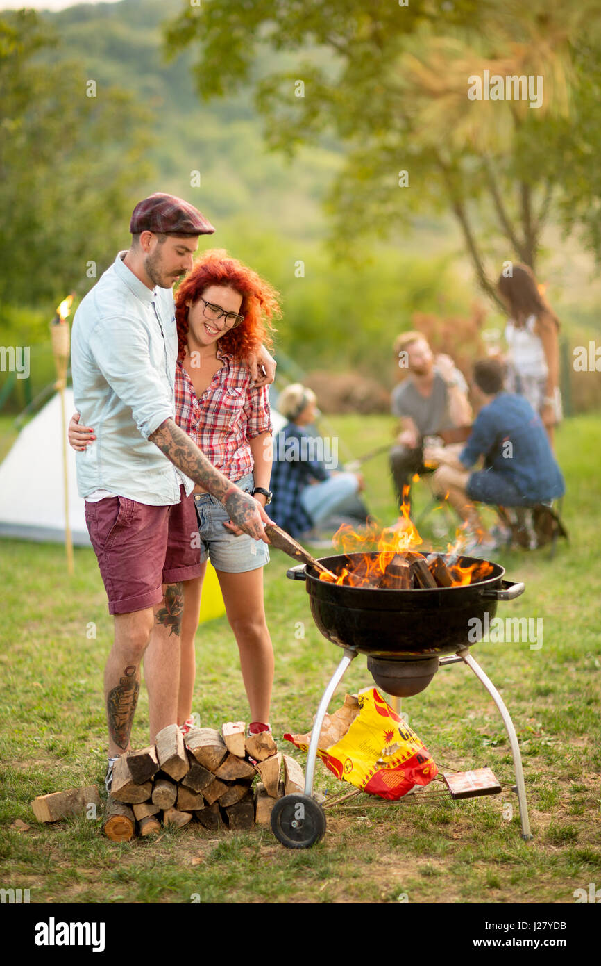 Young curly ginger girl hug boyfriend while he prepare grill fire in ...