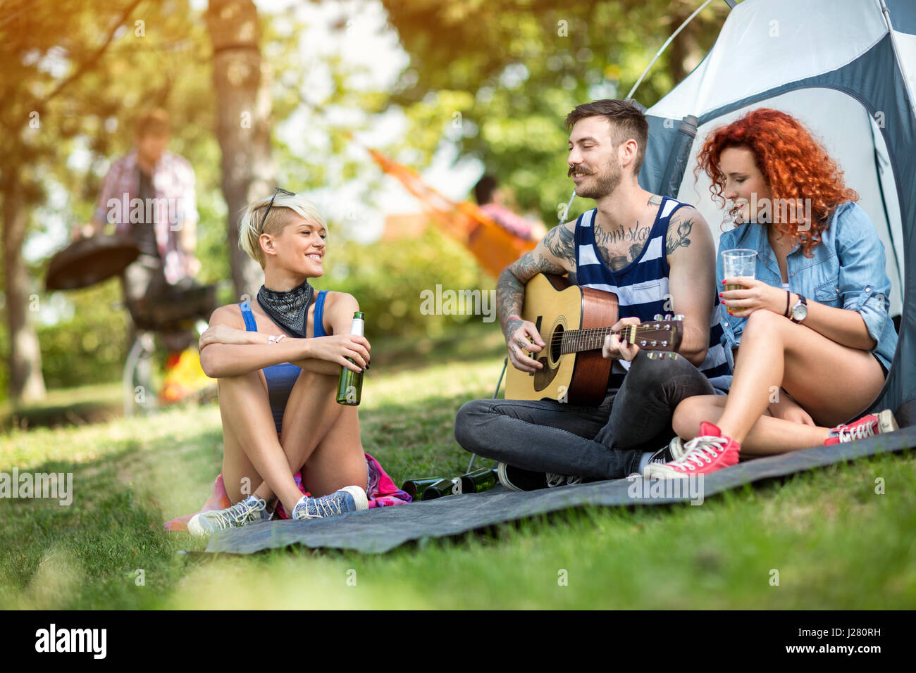 Young people enjoys on excursion with beer and guitar at camp in forest ...