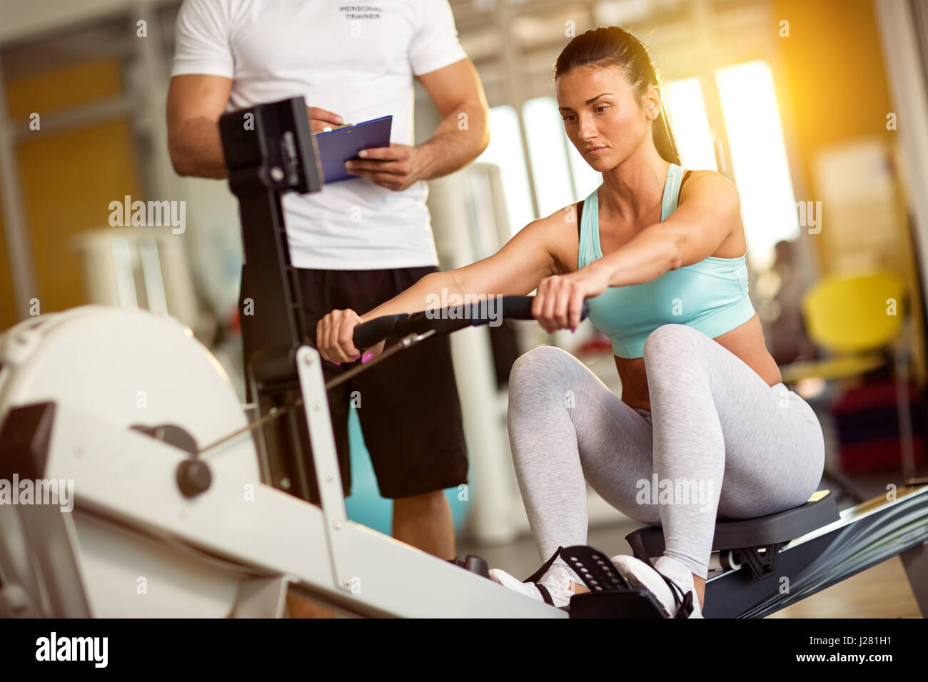 Instructor taking notes of sporty woman working out on row machine in ...