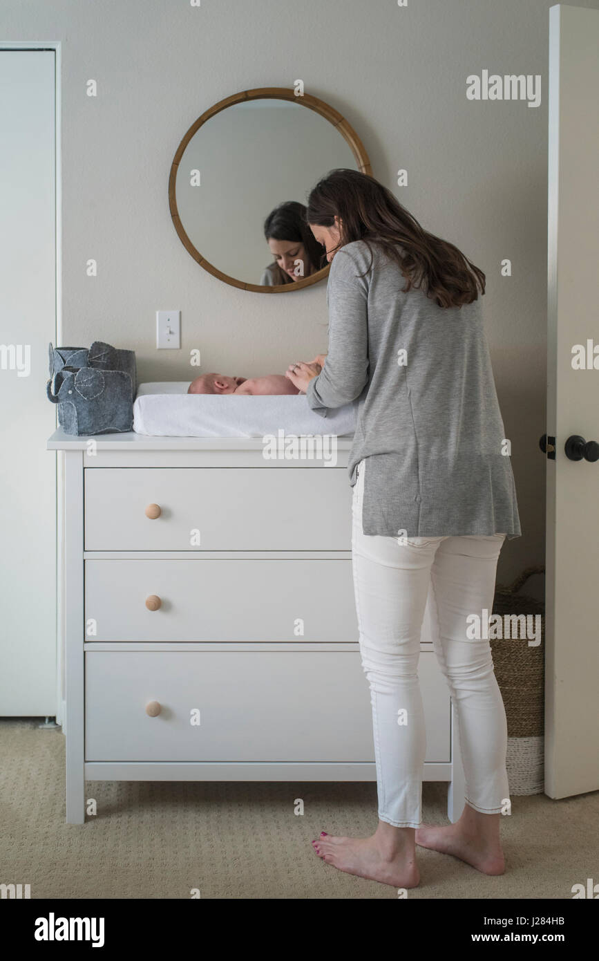 Rear view of mother standing by newborn baby boy lying on sideboard at ...