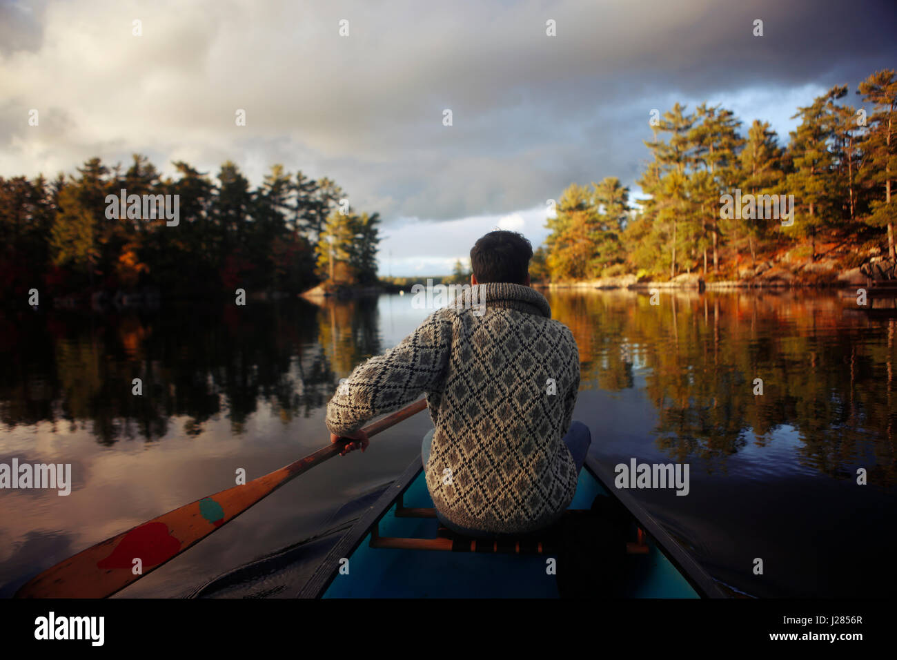 Rear view of man canoeing on lake against cloudy sky during sunset ...