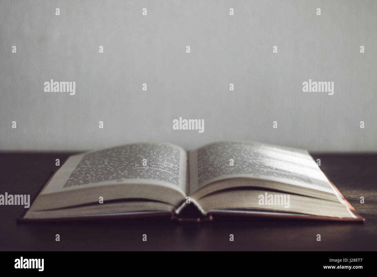 Opened book on an empty wooden table. Behind it is a light background ...