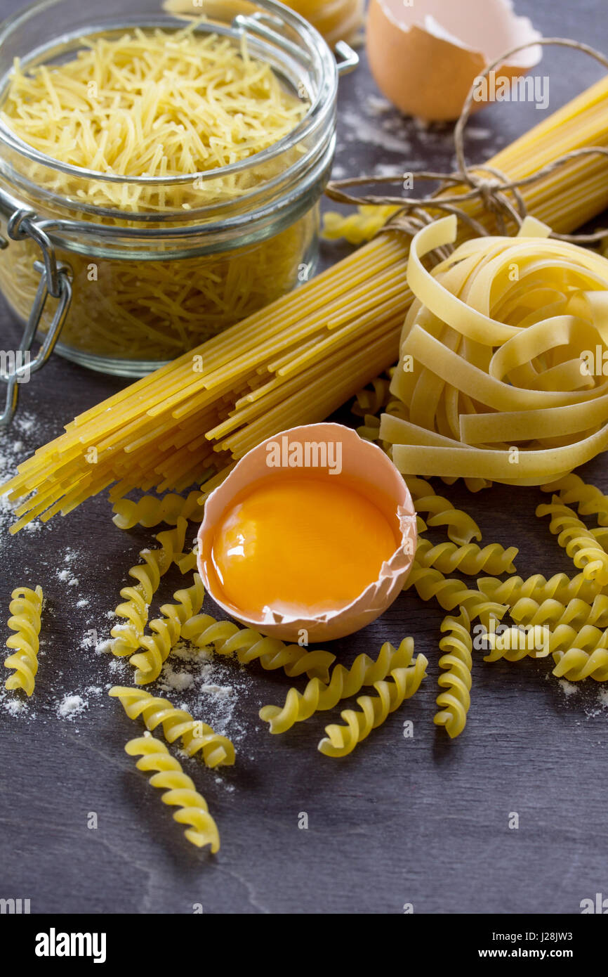 Various types of pasta spaghetti, fusilli, fettuccine and raw egg yolk ...