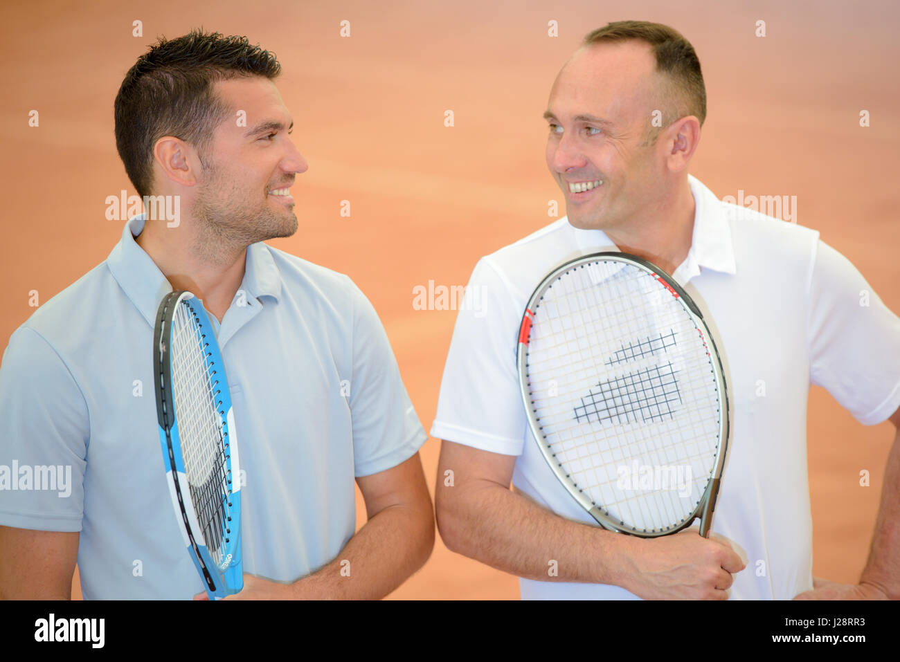 Two men joking together, holding tennis rackets Stock Photo - Alamy
