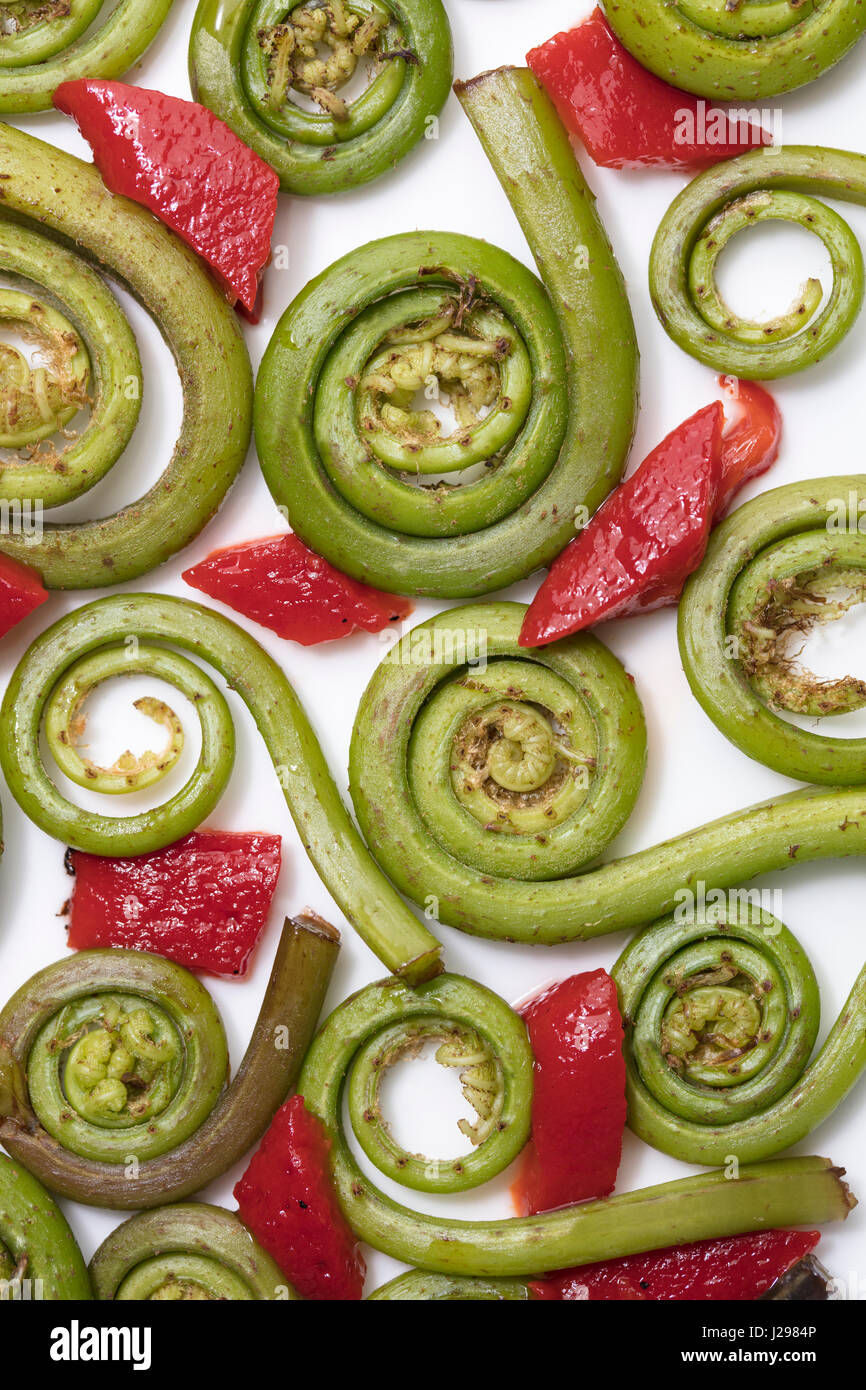 Fiddlehead Ferns and red pepper pieces layed out on a white ceramic ...