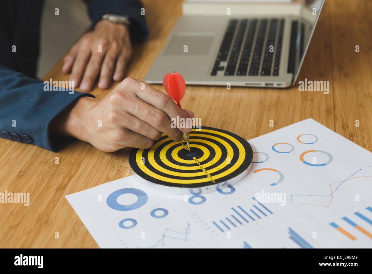 businessman gesturing while holding dart attached to target on ...