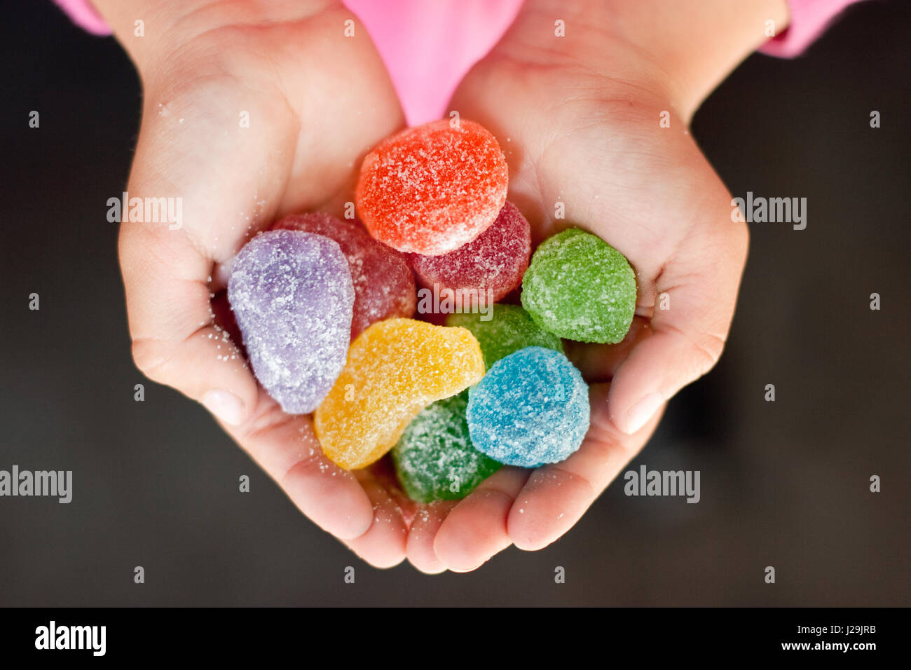 Child hands full of colorful jelly candies with sugar. Dark background ...