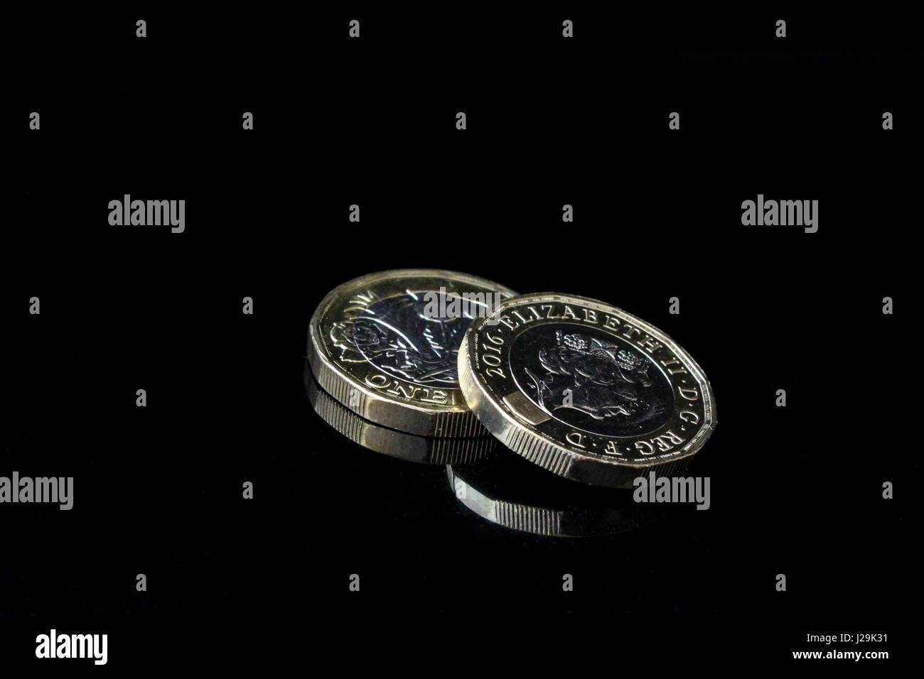 Two new British pound sterling coins, on a reflective black surface ...