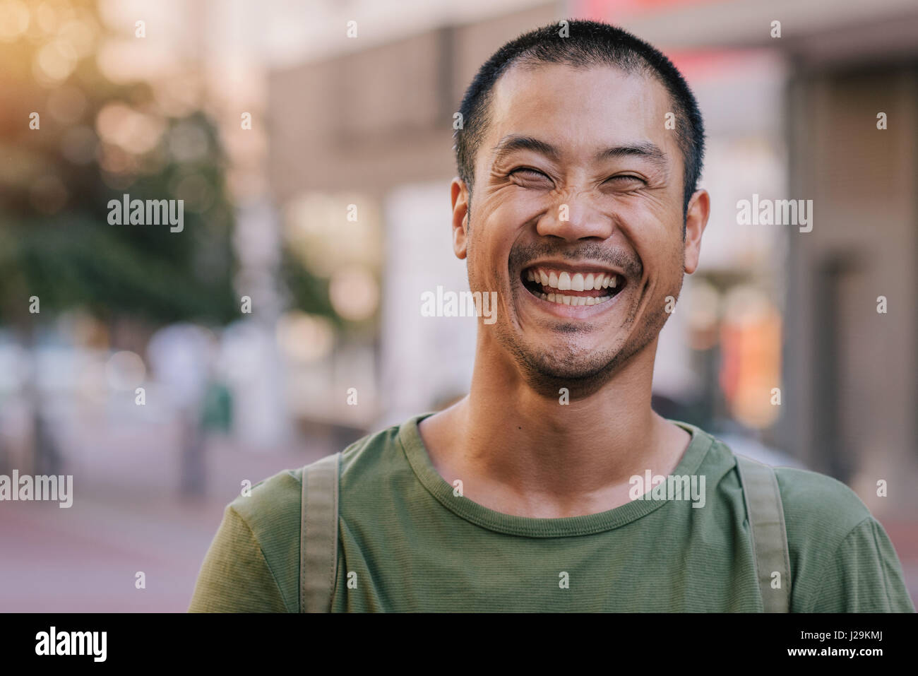Asian man laughing while standing on a city street Stock Photo - Alamy