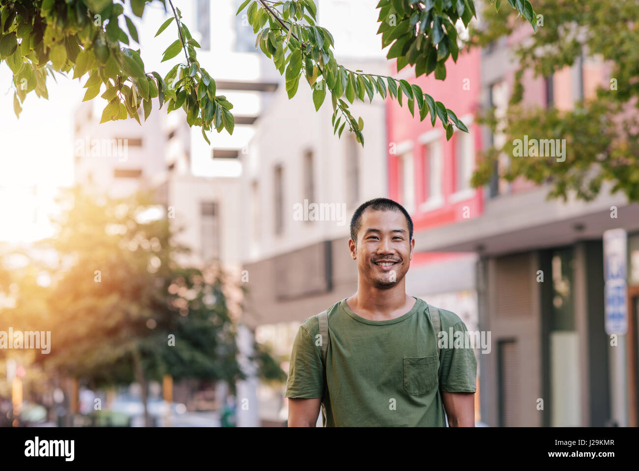 Smiling young Asian man standing on a city street Stock Photo - Alamy