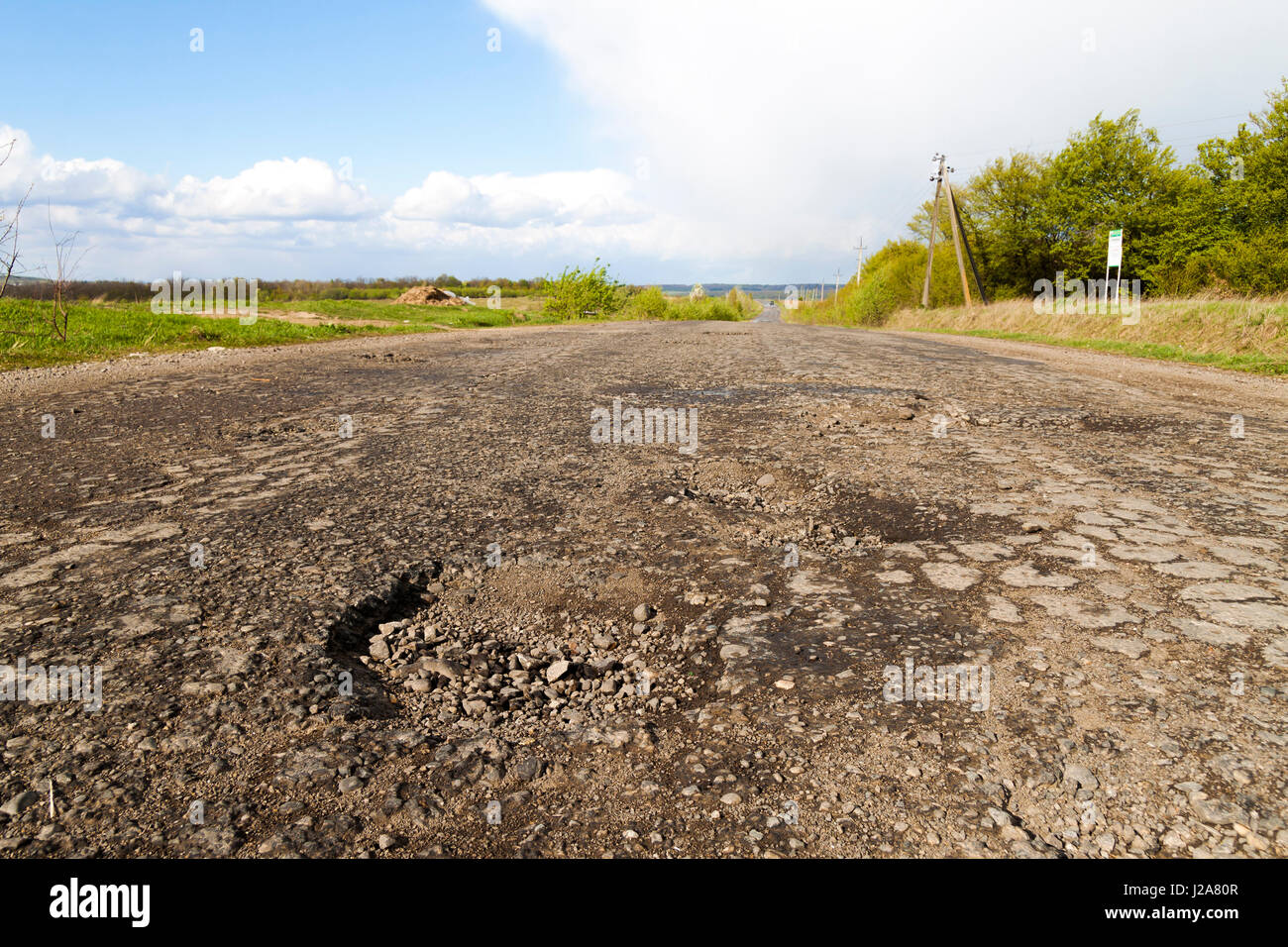 Damaged rural road, cracked asphalt blacktop with potholes and patches ...