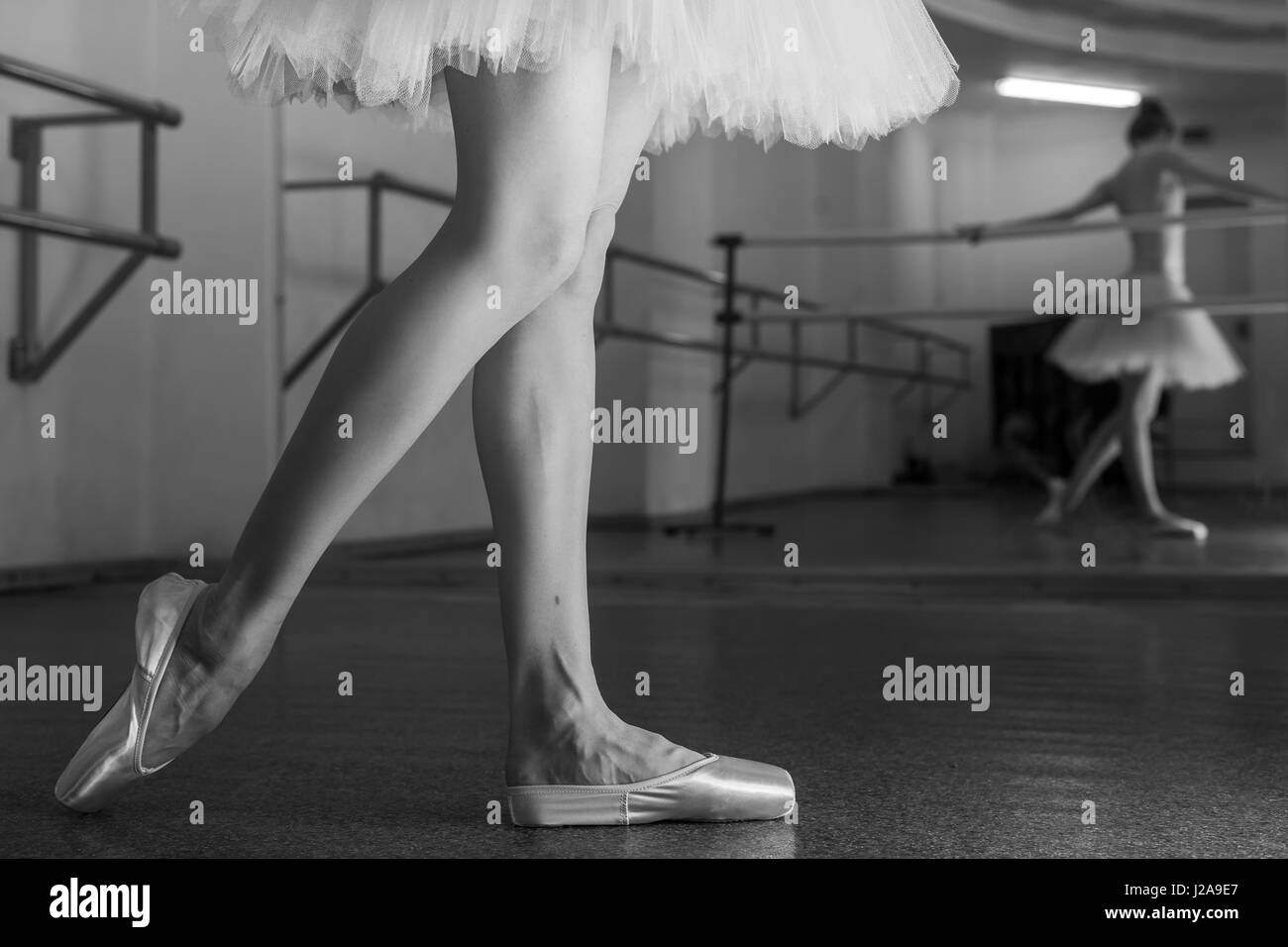 Ballerina in pointes and a pack stretches a foot at the machine ...
