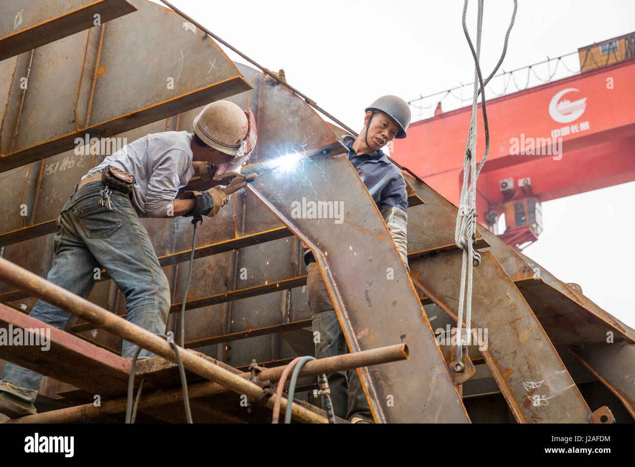 China, Chongqing, Workmen welding steel plates in new ship's hull at ...
