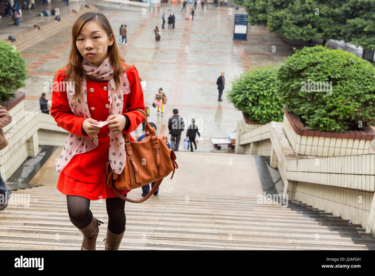 China, Chongqing, Young woman in bright red coat walks up stairs to ...