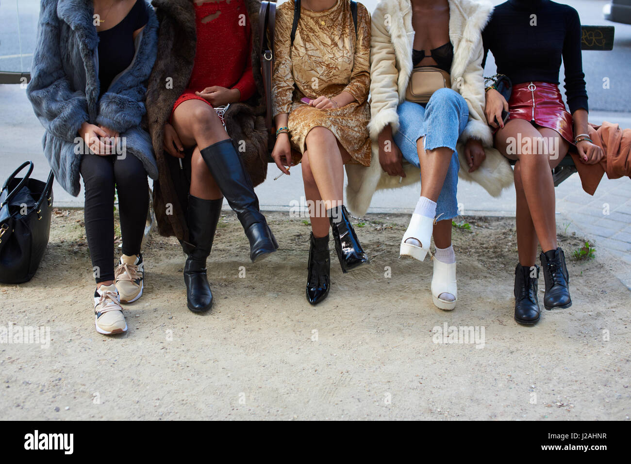 Five fashionable women sitting in a row on a bench, crop Stock Photo ...