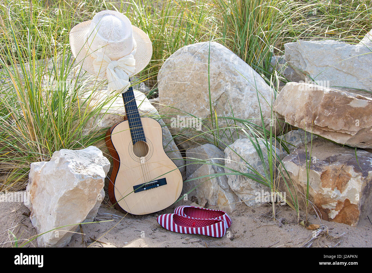 hat on guitar with shoes and rocks in beach sand Stock Photo - Alamy