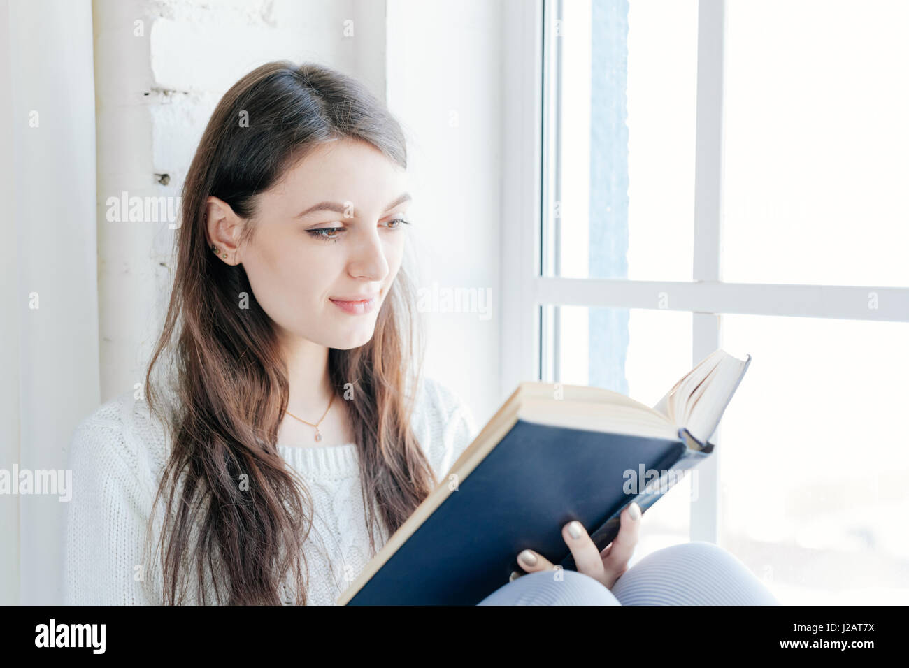 Beautiful girl in white reading book at the window Stock Photo - Alamy