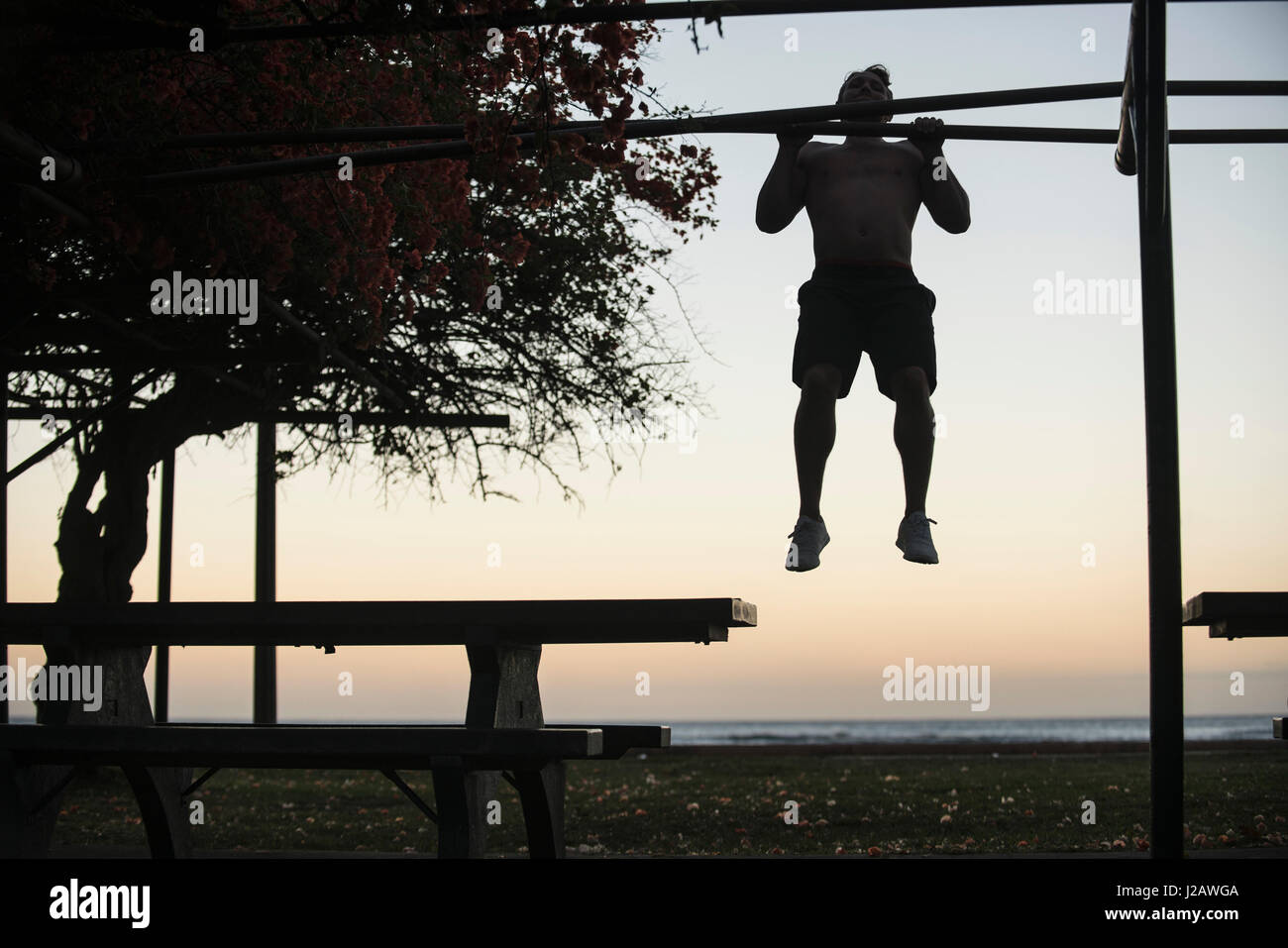 Full length of man doing chin-ups at park against sky at sunset Stock ...