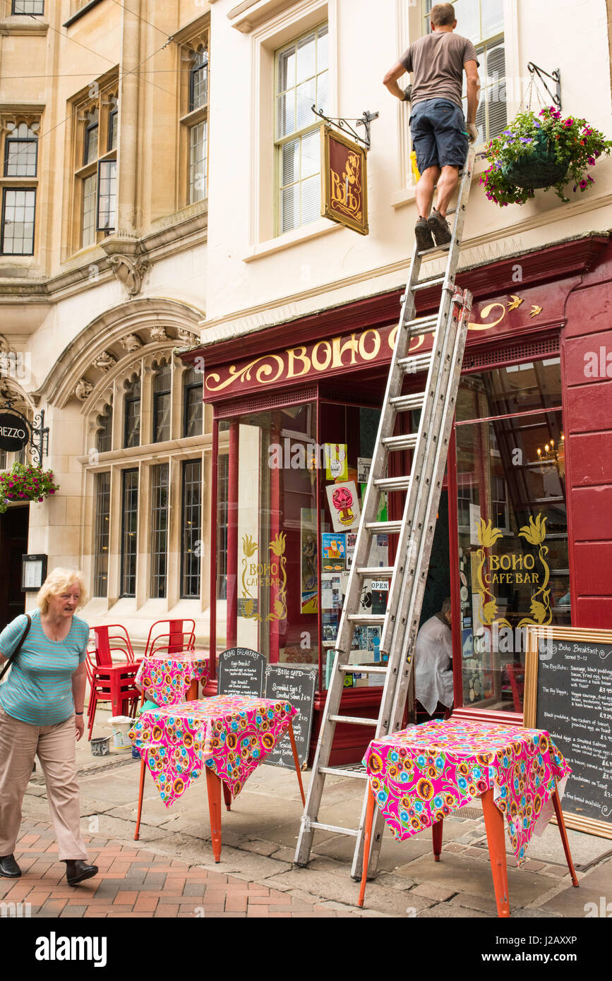 A man cleaning windows at the top of a ladder in the high street in ...