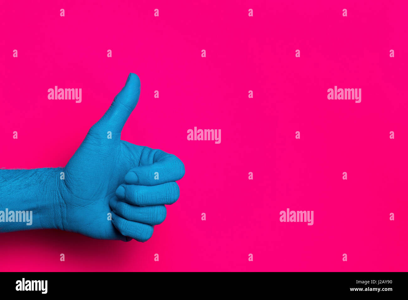 Close-up of blue painted hand showing thumb up against pink background ...