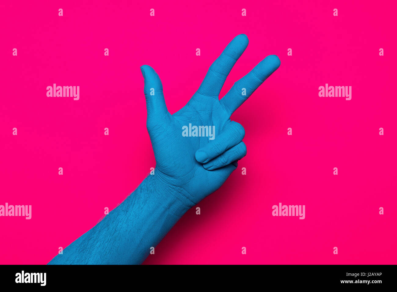Close-up of blue painted hand showing peace sign against pink ...