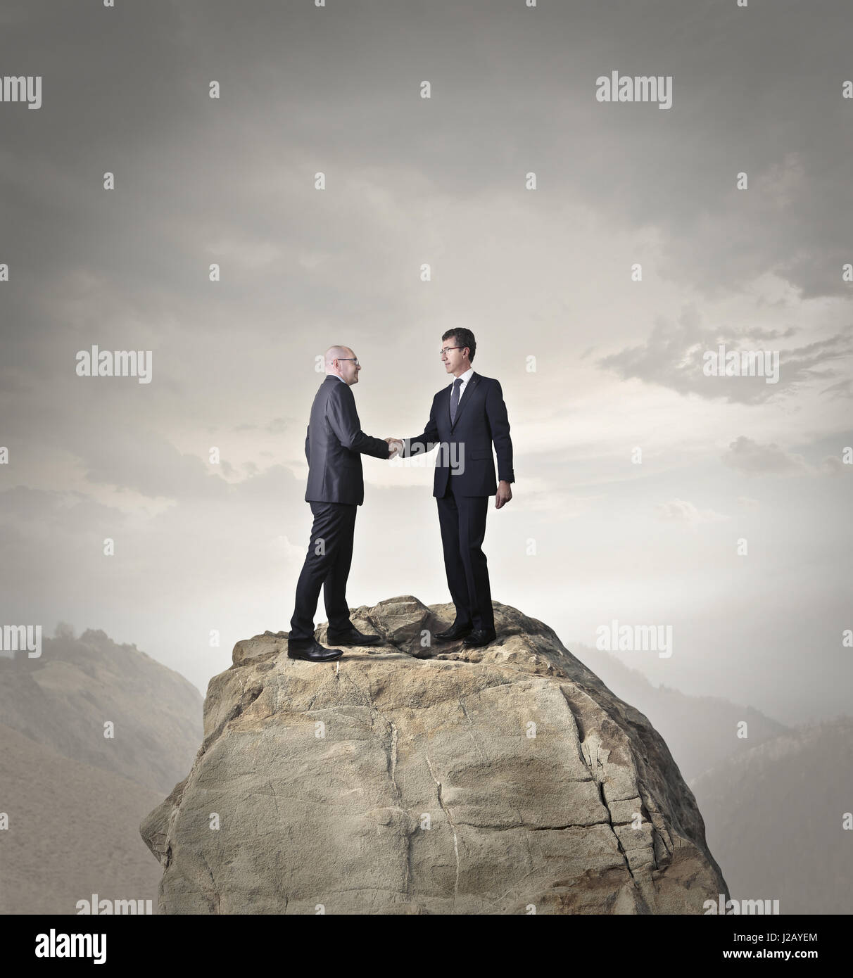 2 businessman shaking hands on rock Stock Photo - Alamy