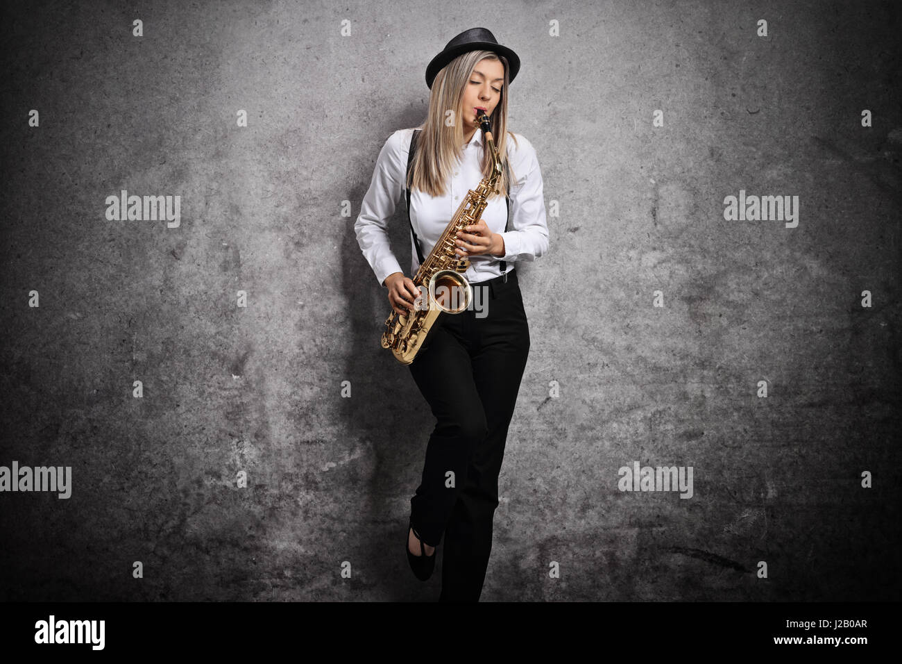 Attractive young woman playing a saxophone and leaning against a rusty ...