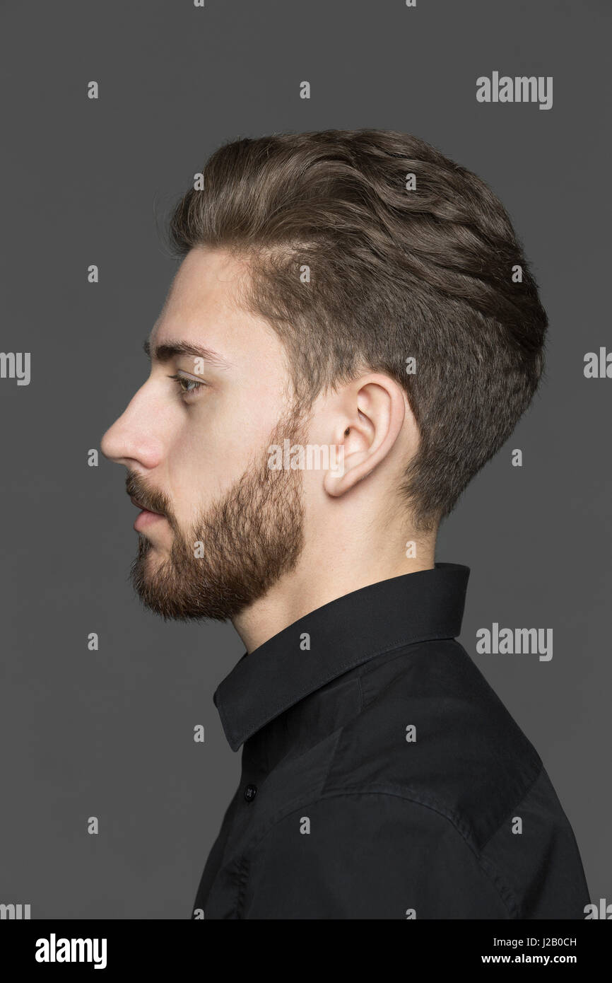Side view of young man looking away against gray background Stock Photo ...