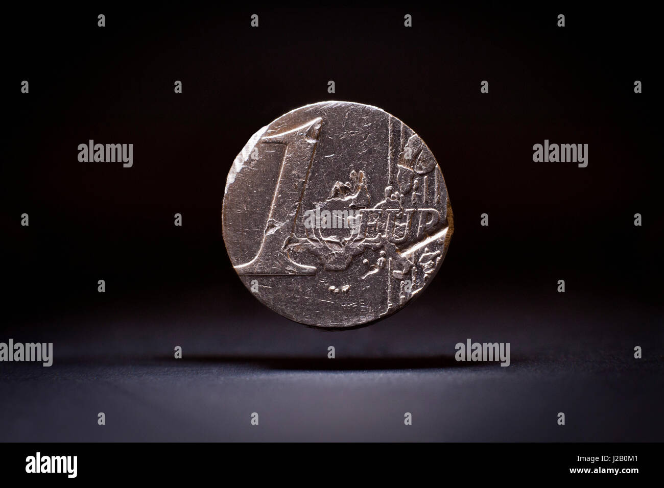 Close-up of damaged one euro coin levitating against black background ...