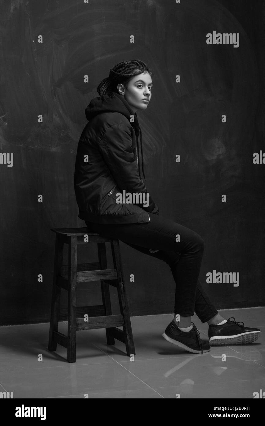 Beautiful fashion model sitting on stool against wall Stock Photo - Alamy