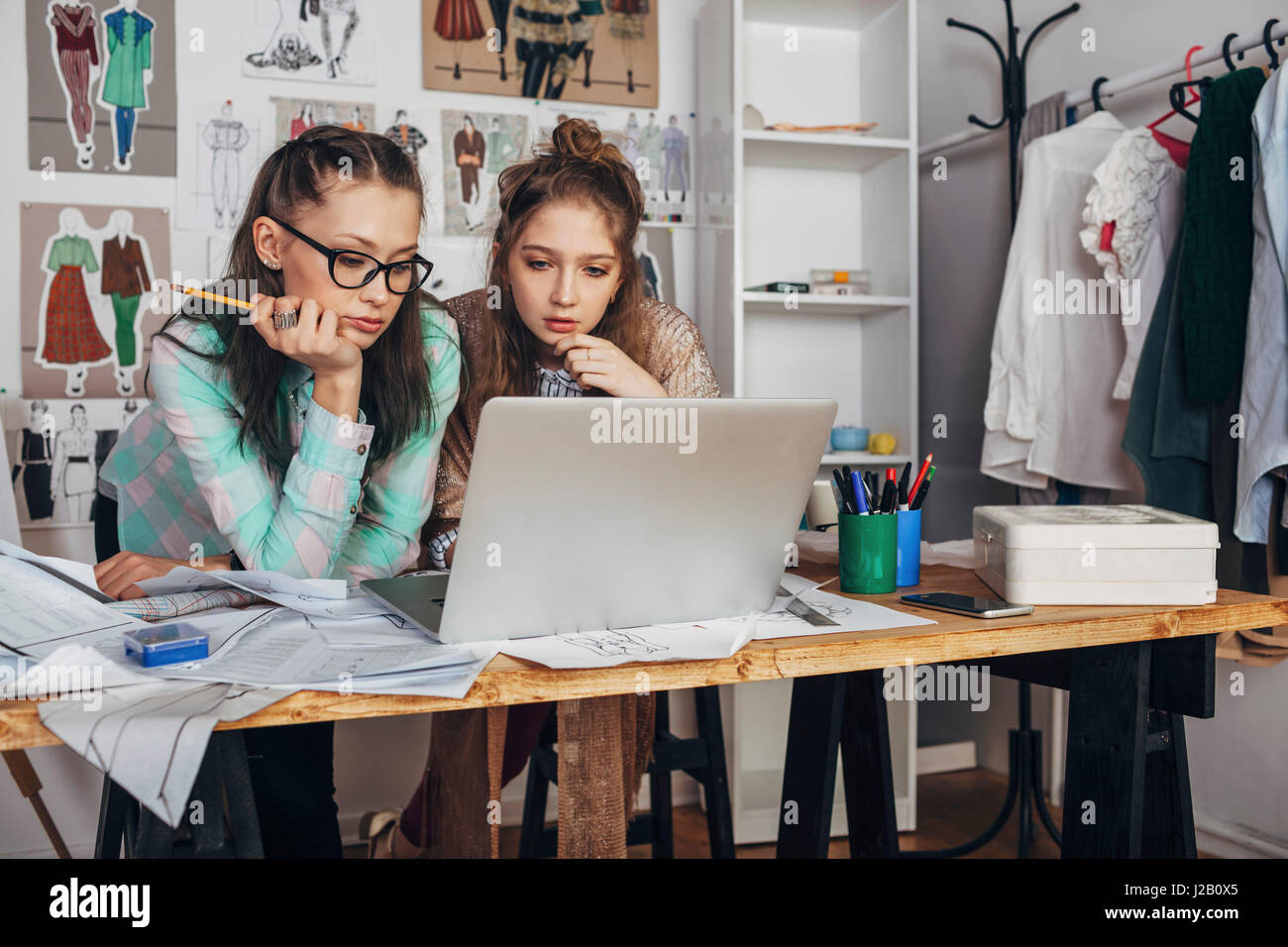 Female trainee and beautiful fashion designer using laptop on workbench ...