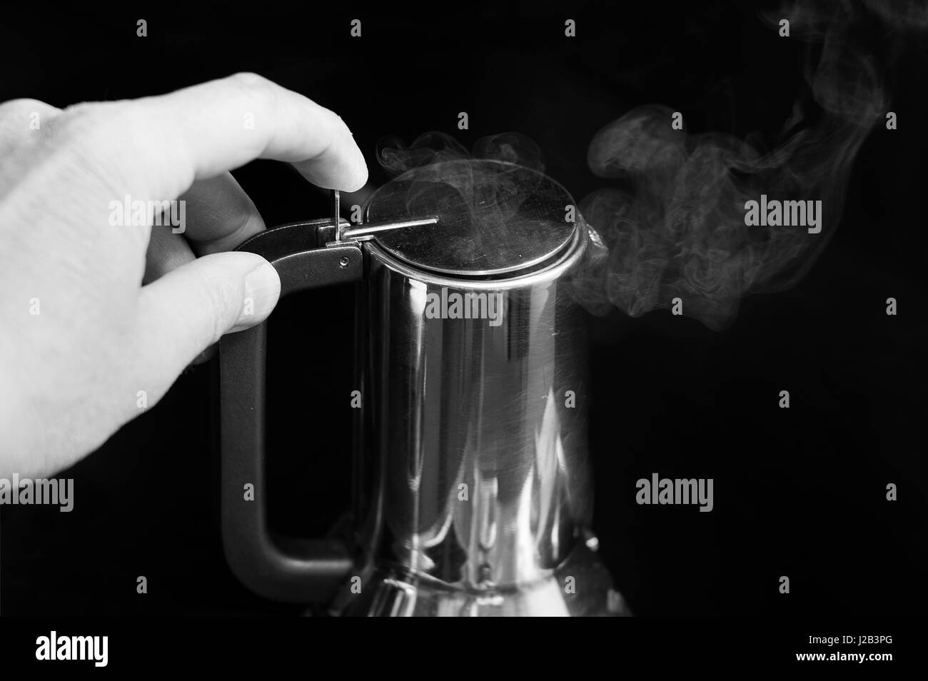 Human hand holding a coffee maker with steam coming out, in black and ...