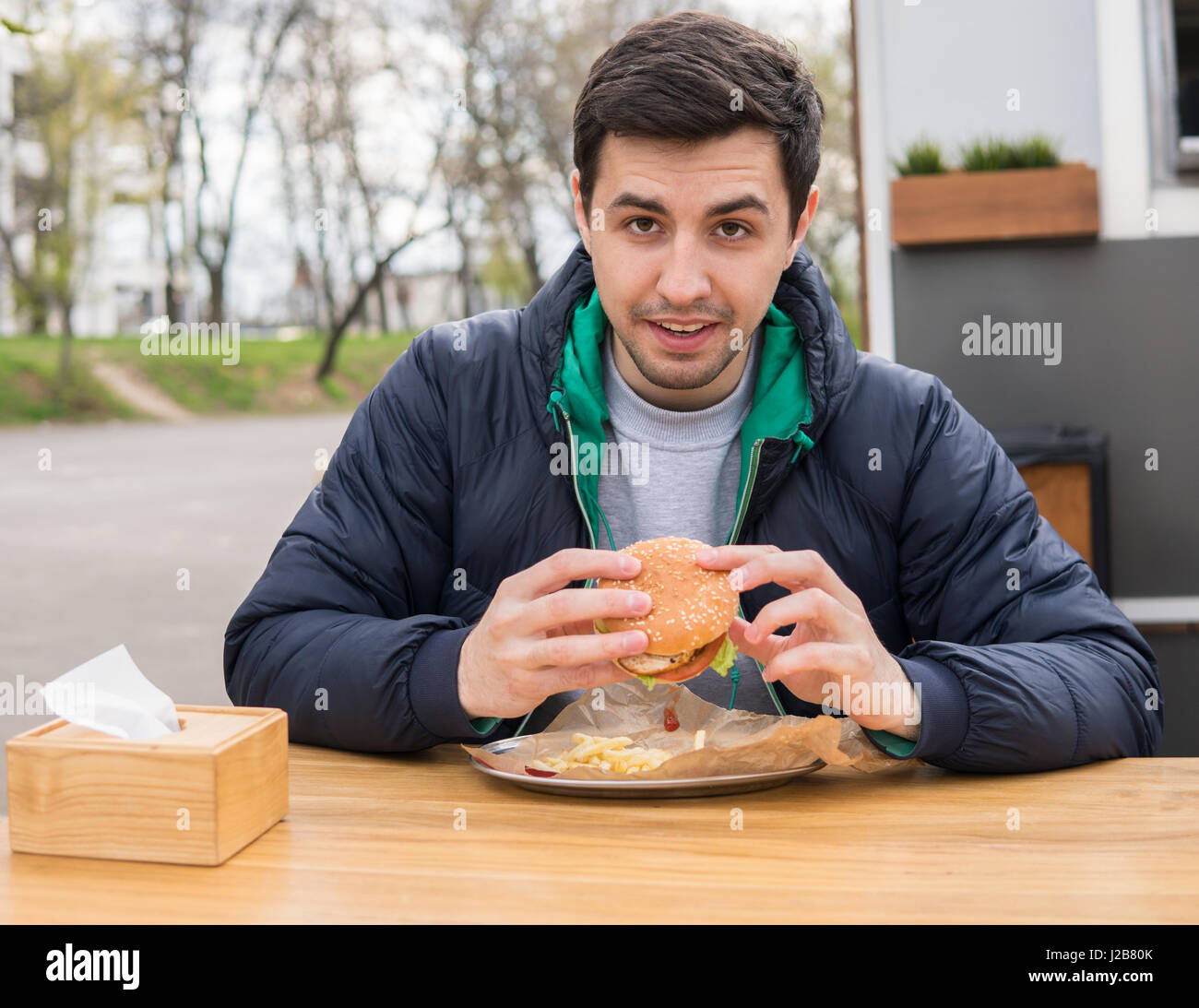 A portrait of young man eating a burger in street food cafe Stock Photo ...