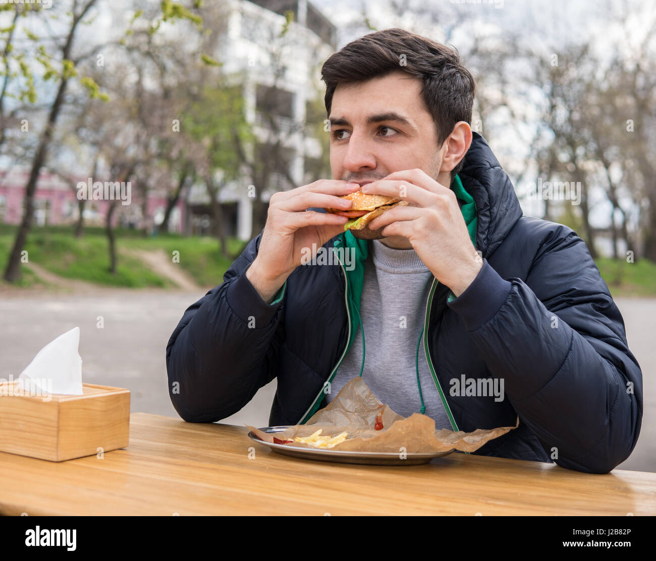 A young man bites off a burger in a snack bar Stock Photo - Alamy