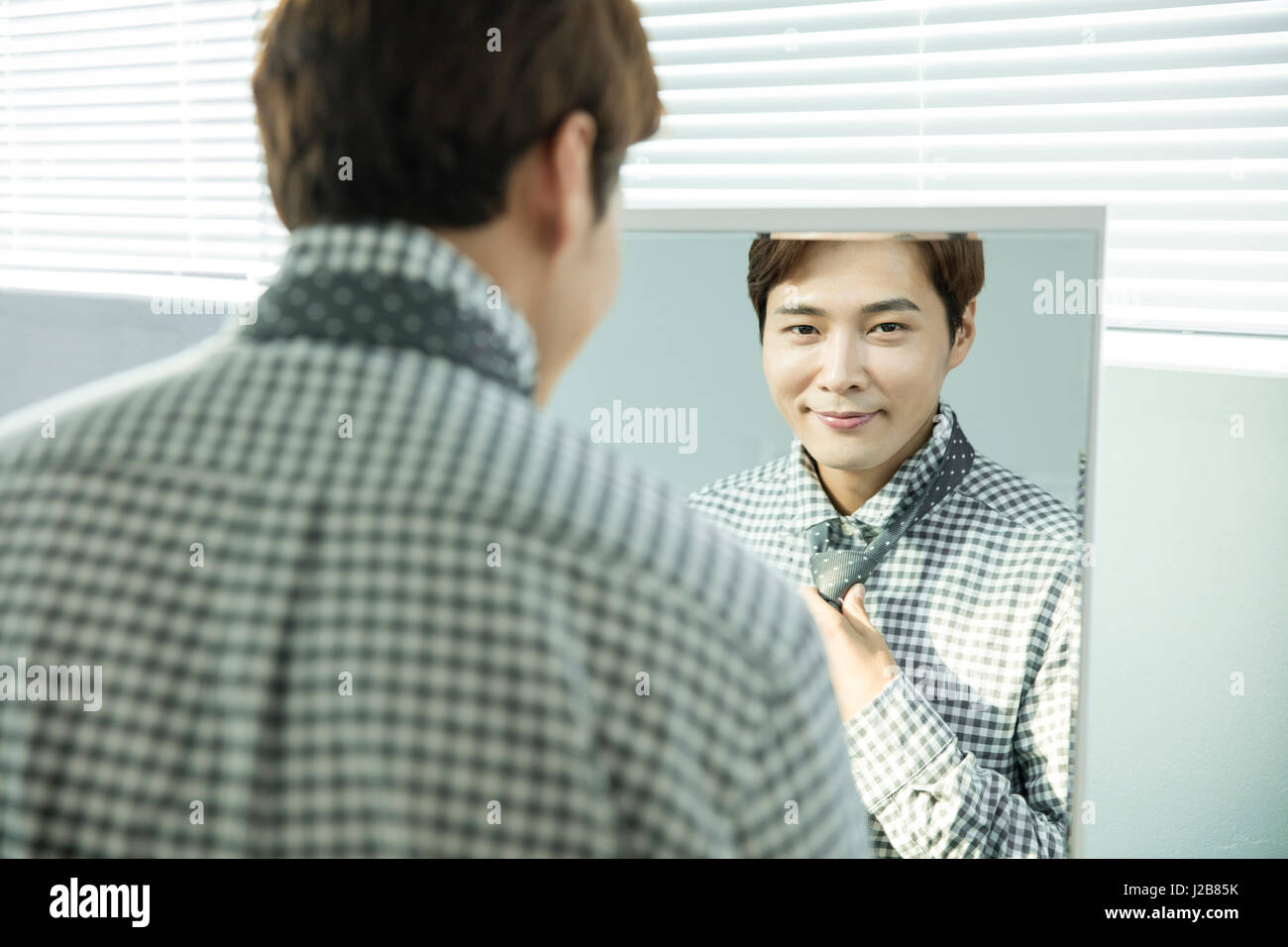 Smiling businessman looking in mirror wearing tie Stock Photo - Alamy