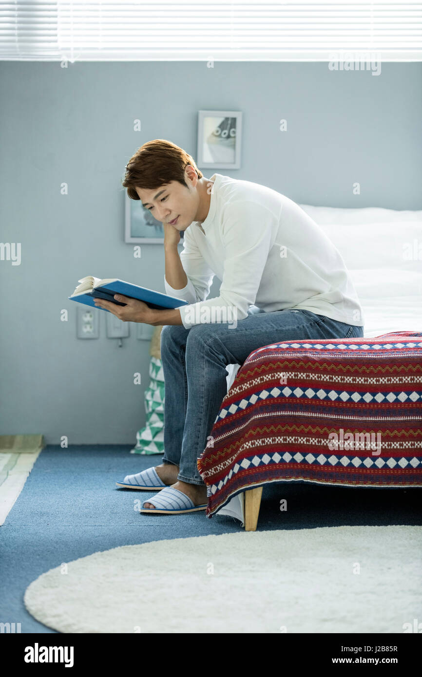 Man sitting on bed reading a book Stock Photo - Alamy