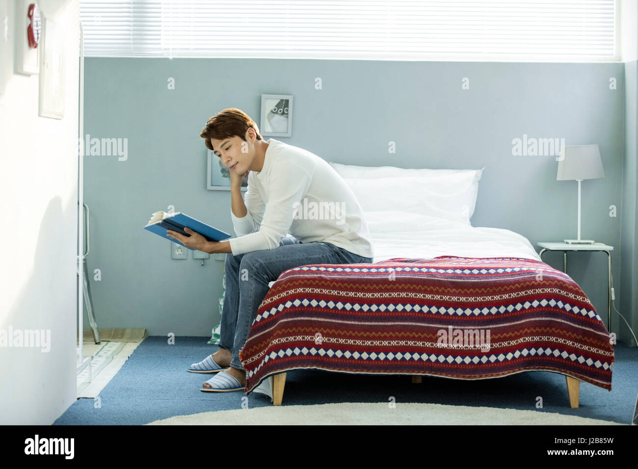 Man reading a book sitting on bed Stock Photo - Alamy