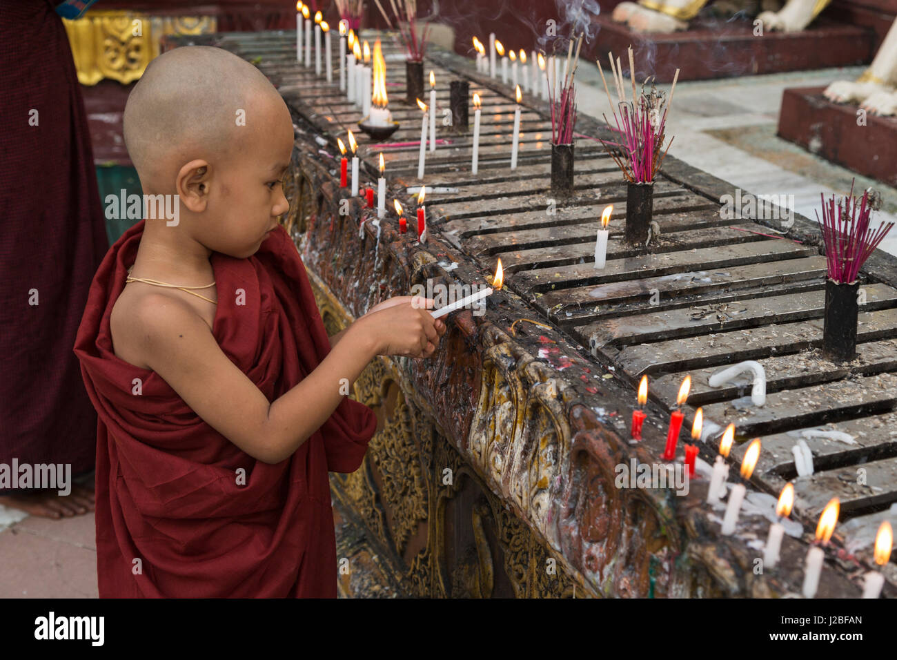 Myanmar, Yangon. A young boy monk holding an offering candle and ...