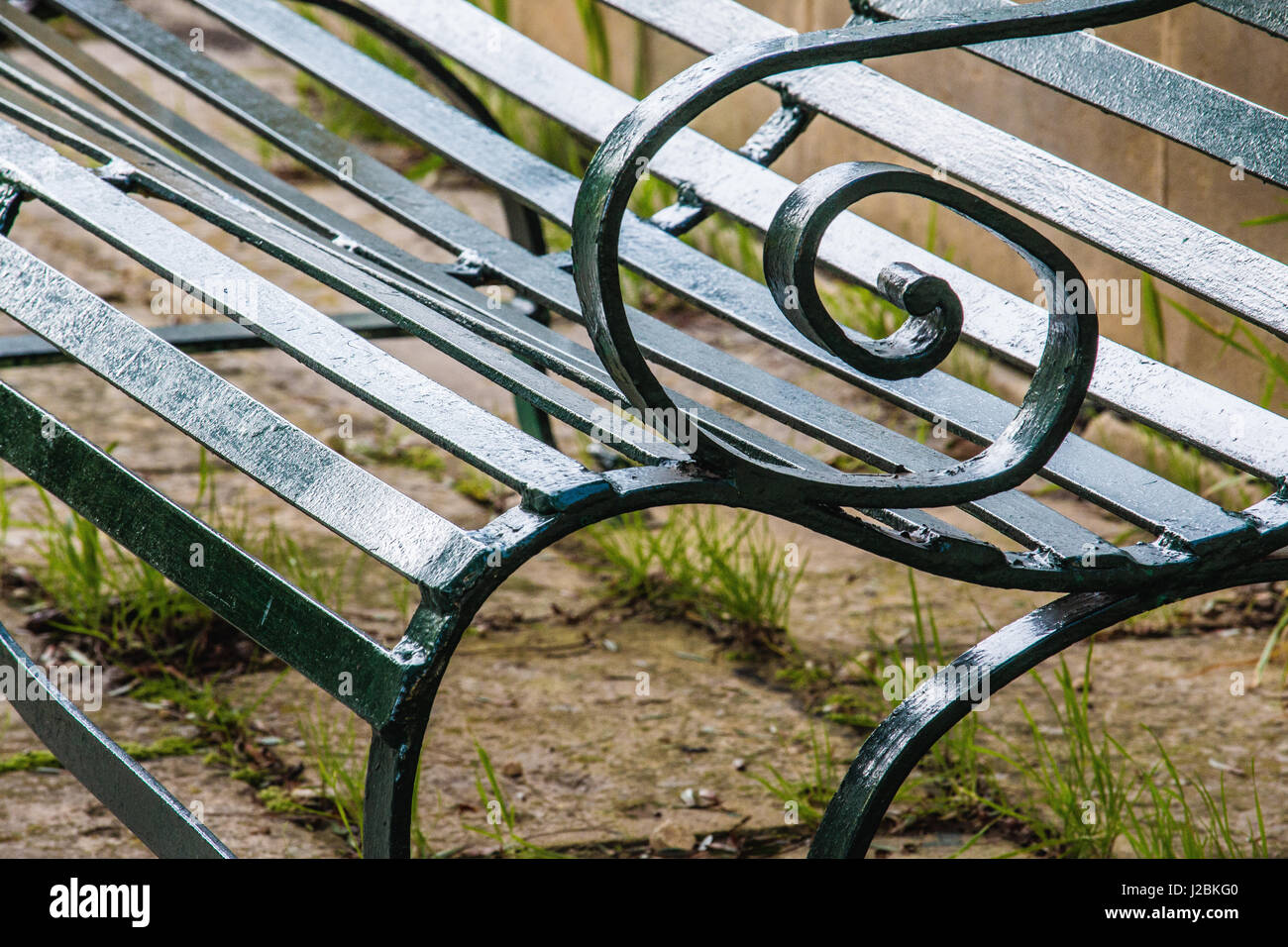 Close up detail of a green painted metal bench in a park. Curved arm ...
