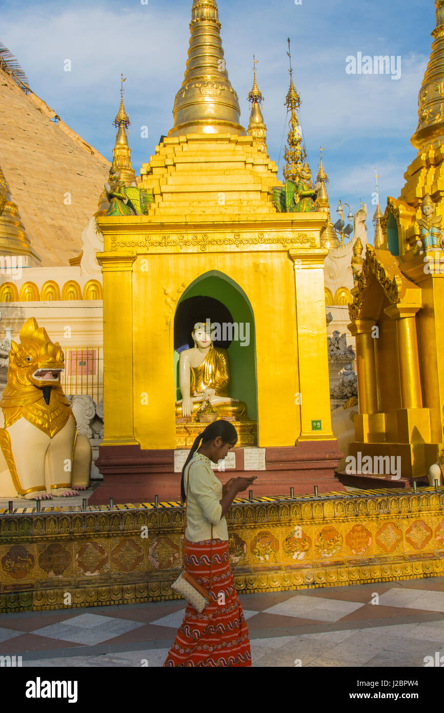 Myanmar. Yangon. Shwedagon Pagoda. Woman checking her phone as she walks through the pagoda ...